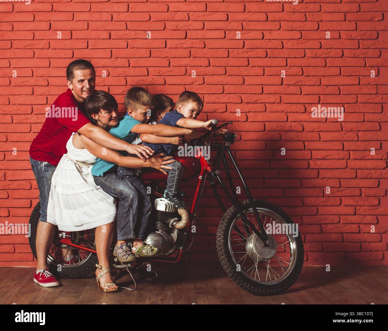 Big and happy family on motorcycle at red background of brick wall ...