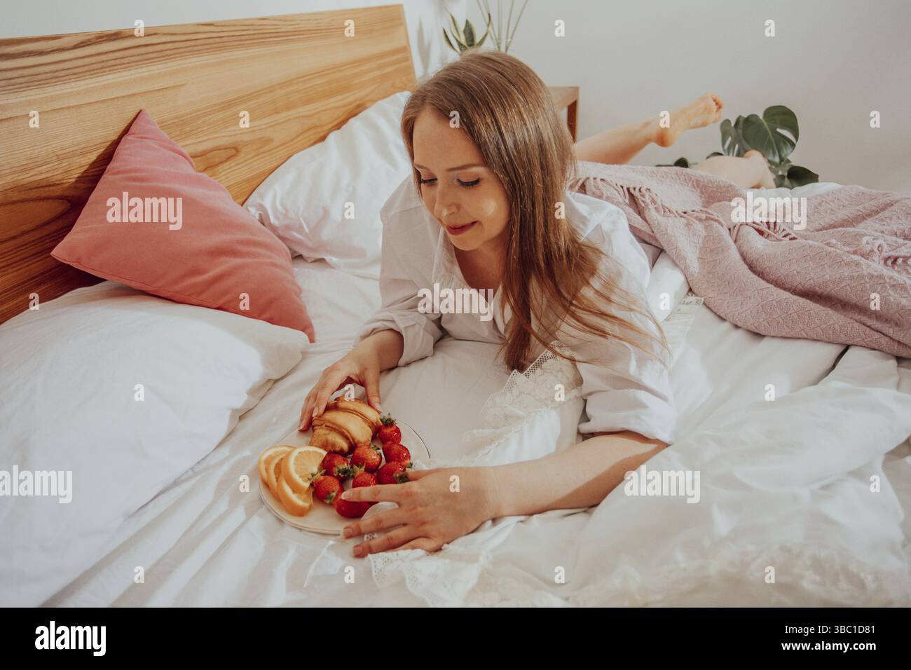 Breakfast. Young woman eating in bed small tasty breakfast of fruits ...