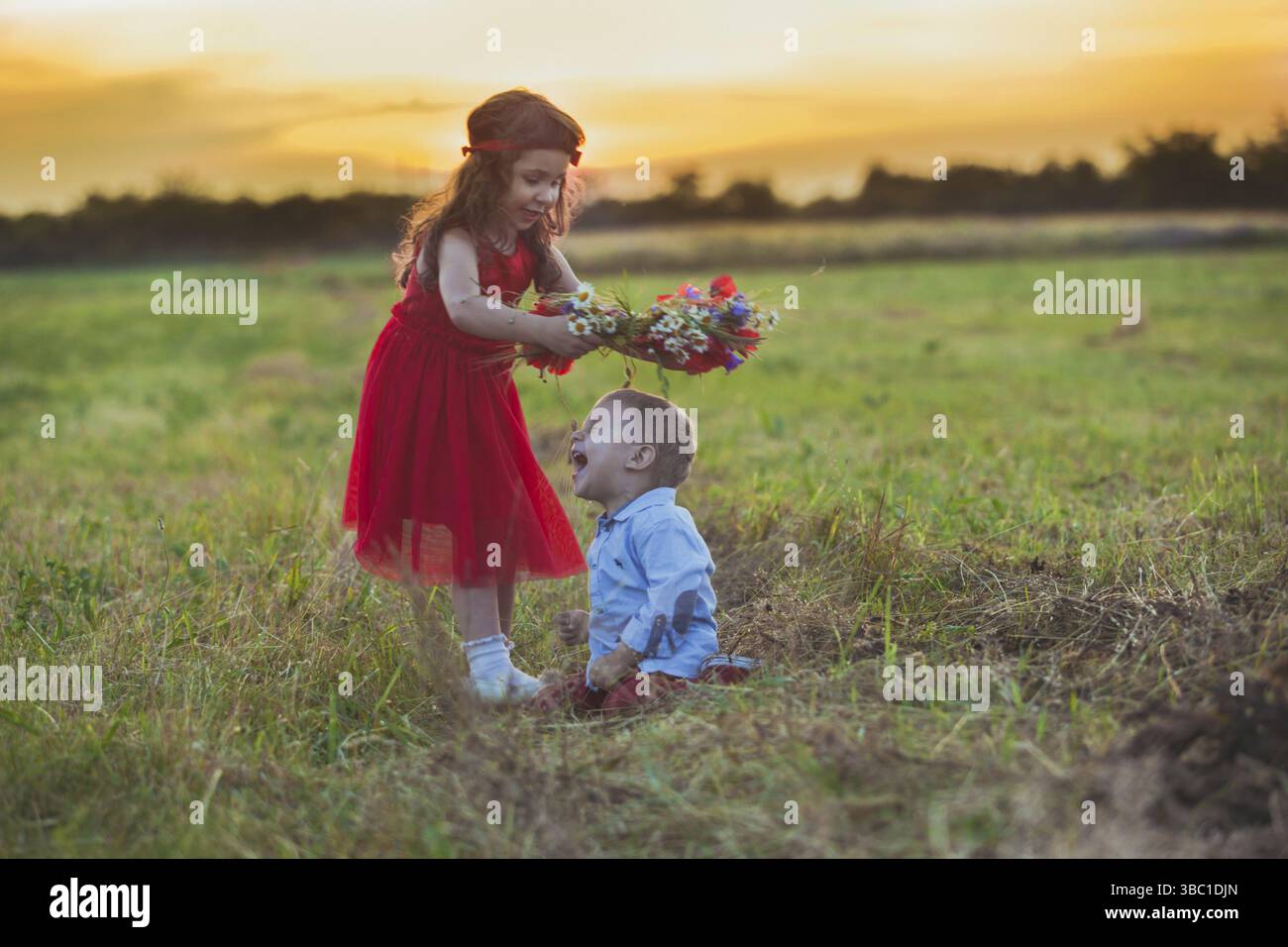Cute girl is trying to put a floral wreath on her brother head Stock ...