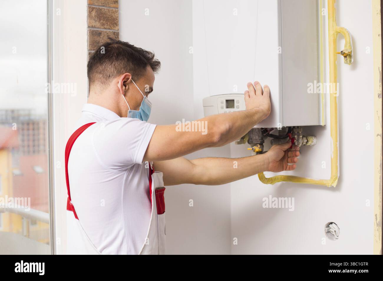 The side view of a young plumber installing a boiler. The man wearing ...