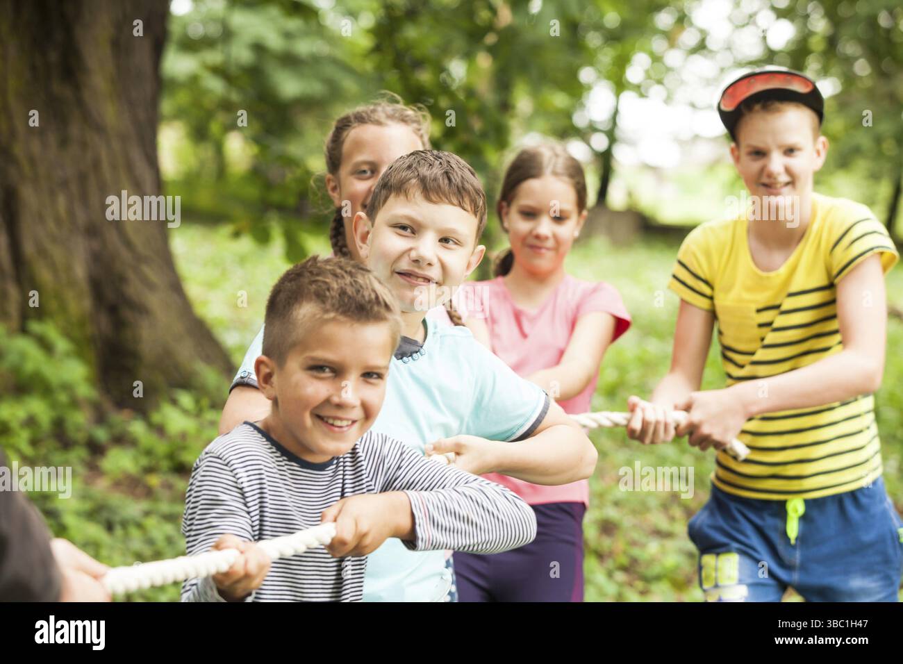 Group of happy smiling kids playing tug-of-war with rope in green park ...
