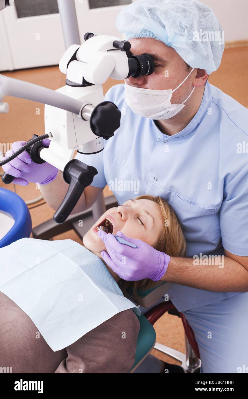 The dentist in the mask and gloves examines the patient's teeth ...