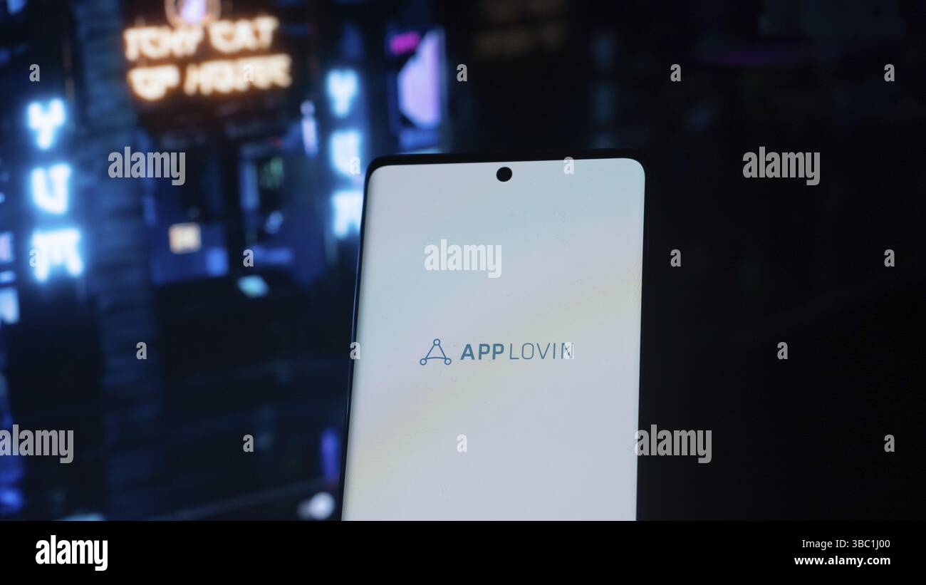 Silhouette of Hand Holding Phone with AppLovin (APP) Logo in AppLovin Website on Computer Screen ...
