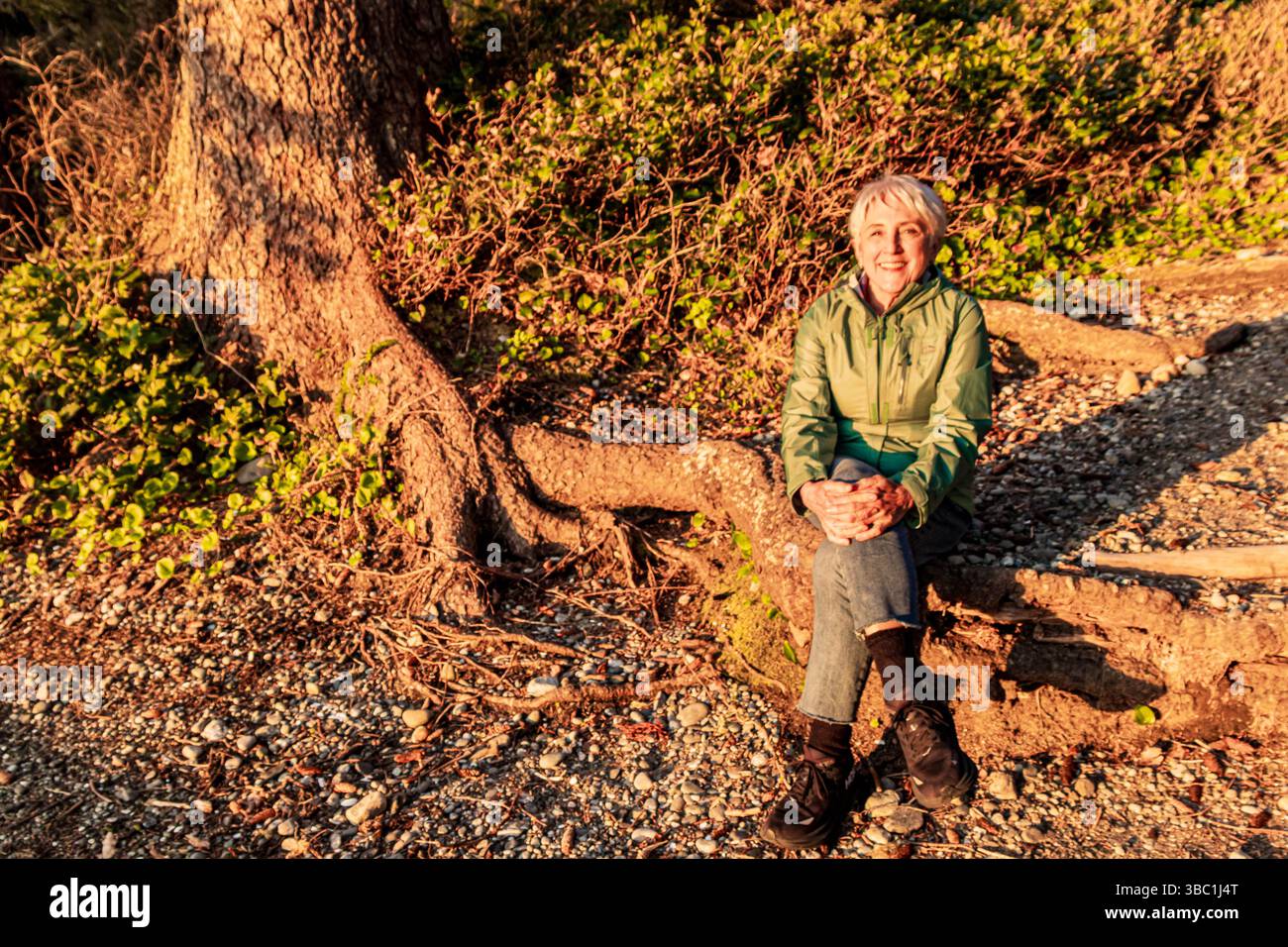 Senior woman sitting on log facing camera. Healthy, active senior in ...