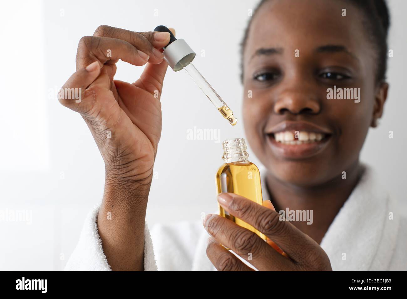 Beautiful black girl dropping argan oil into bottle holding pipette ...