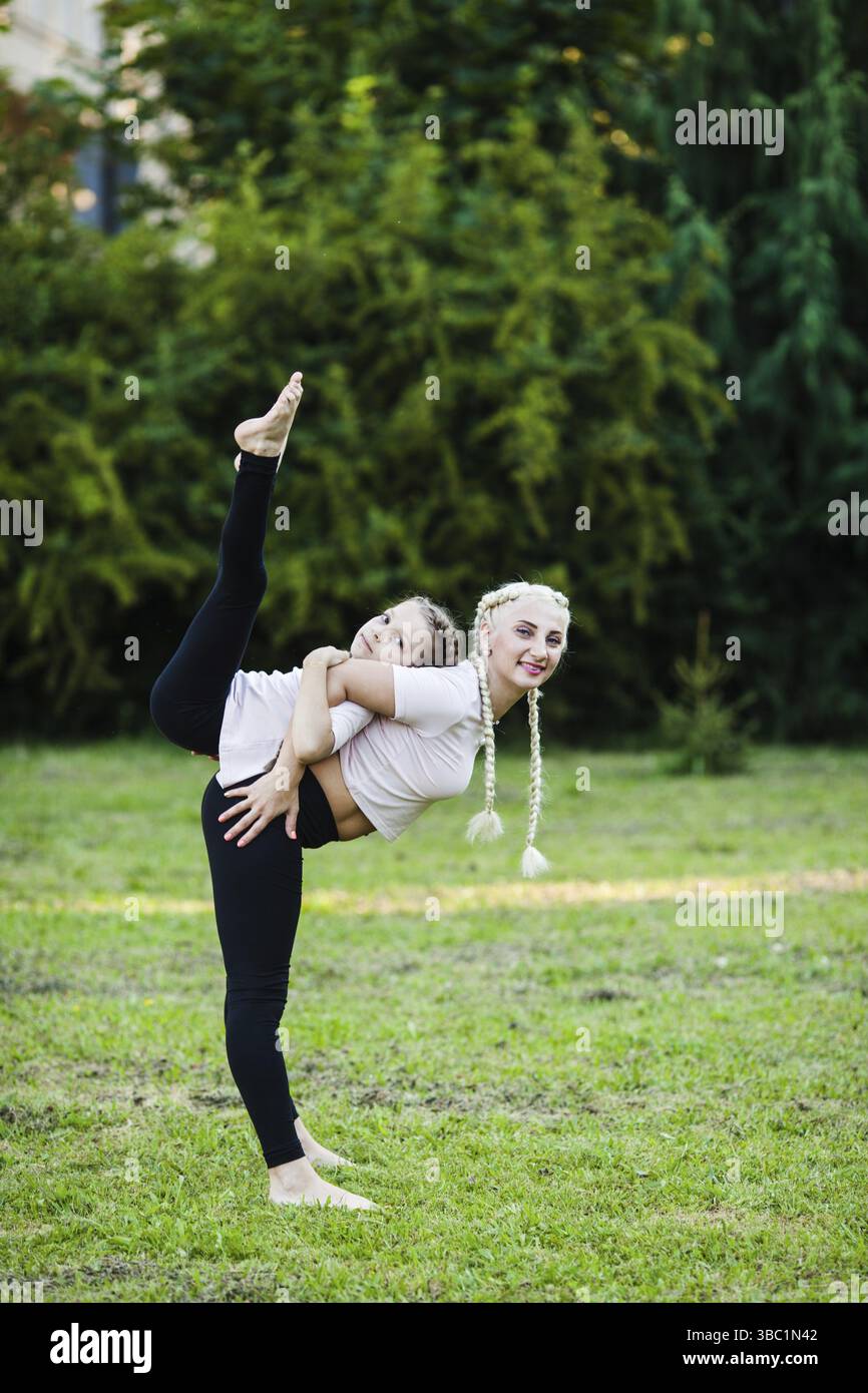 Sporty mother and daughter stretching on grass in a park, daughter ...