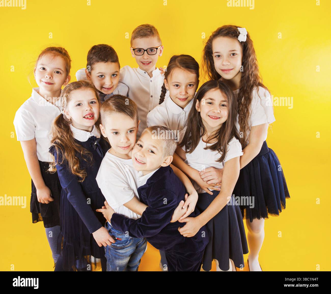 The little smiling pupils are hugging while standing at the yellow ...