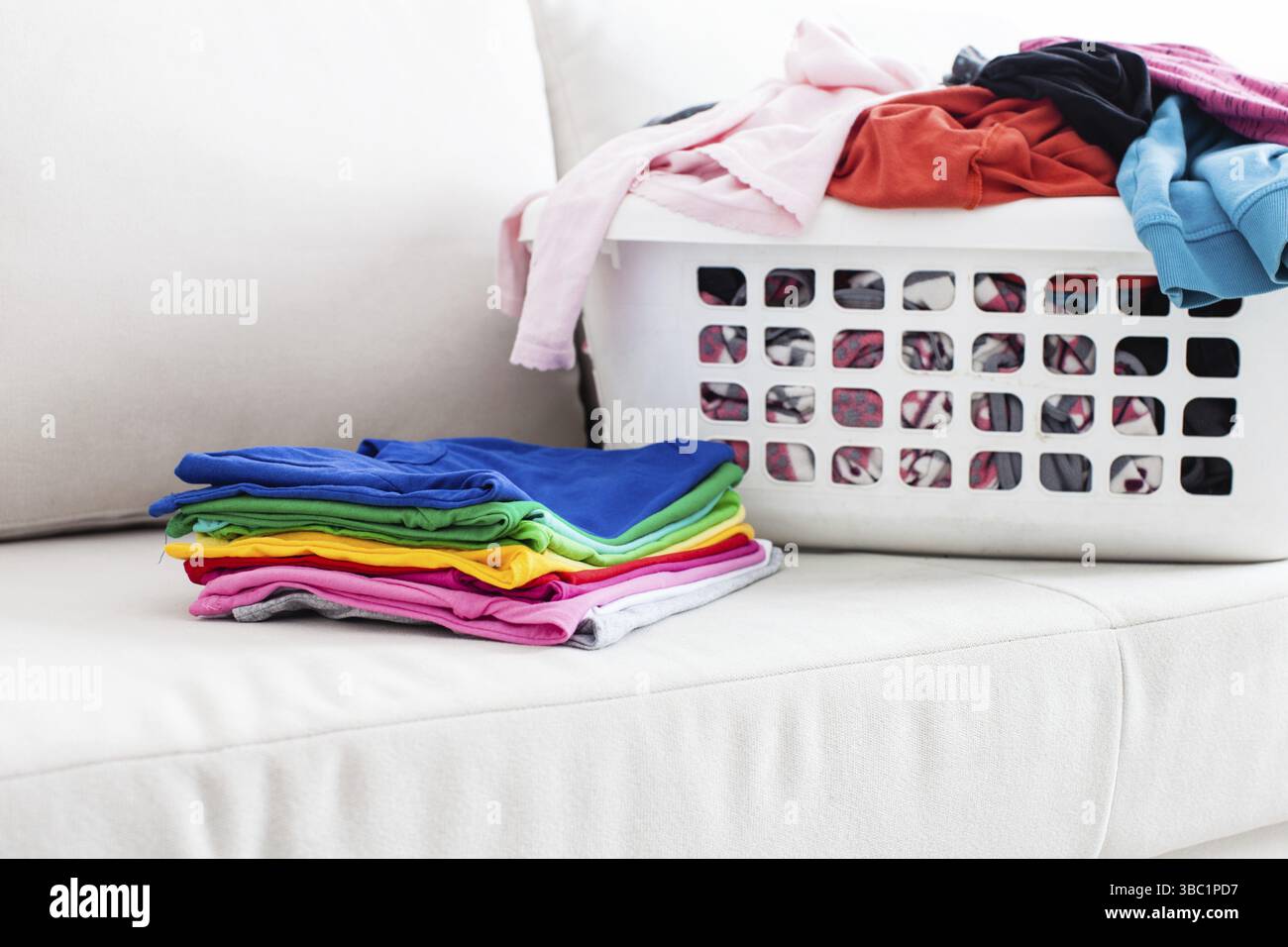 Washed clothes in a basket and stack of clean linen on the sofa Stock ...