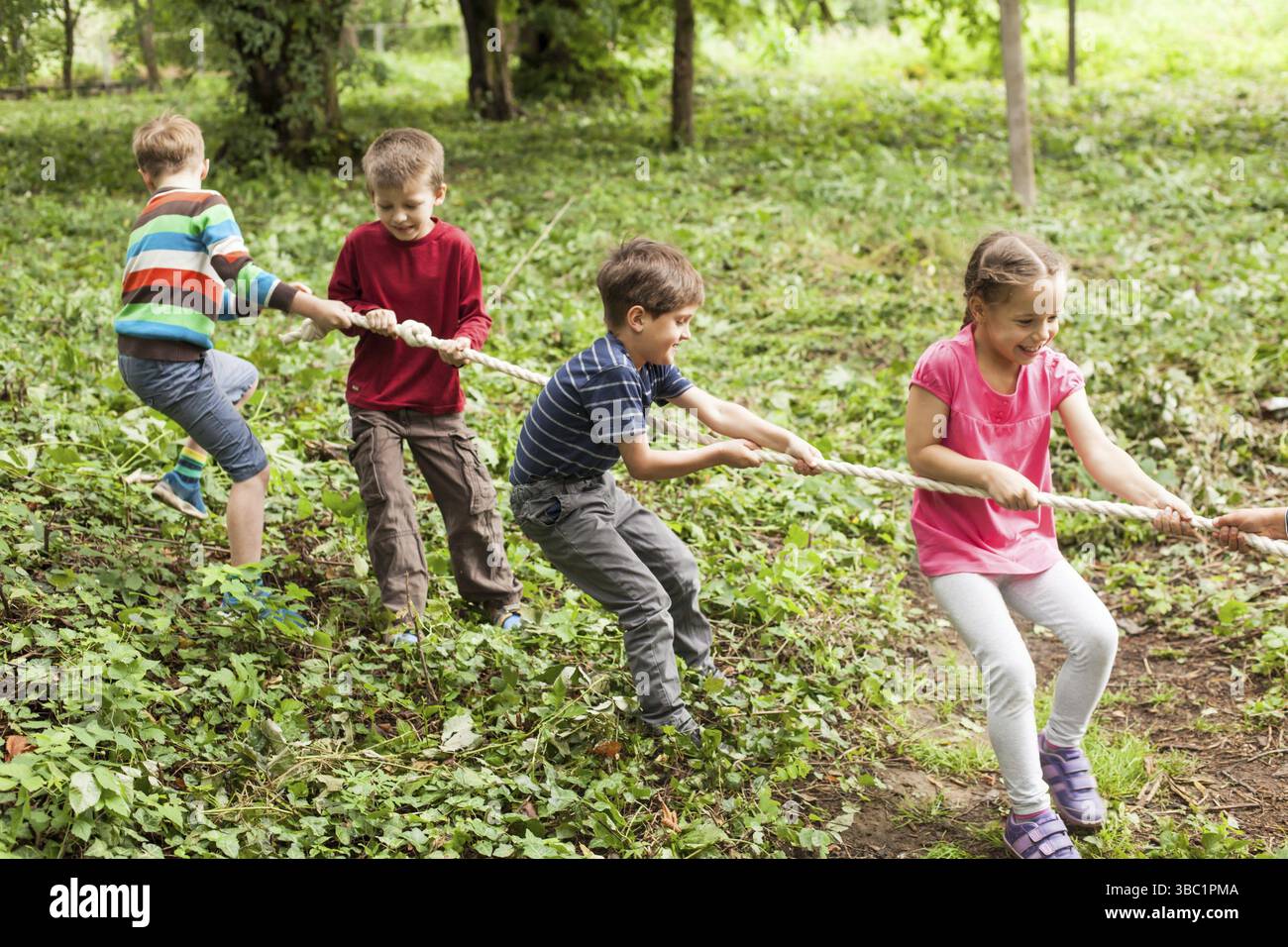 Group of happy smiling kids playing tug-of-war with rope in green park ...