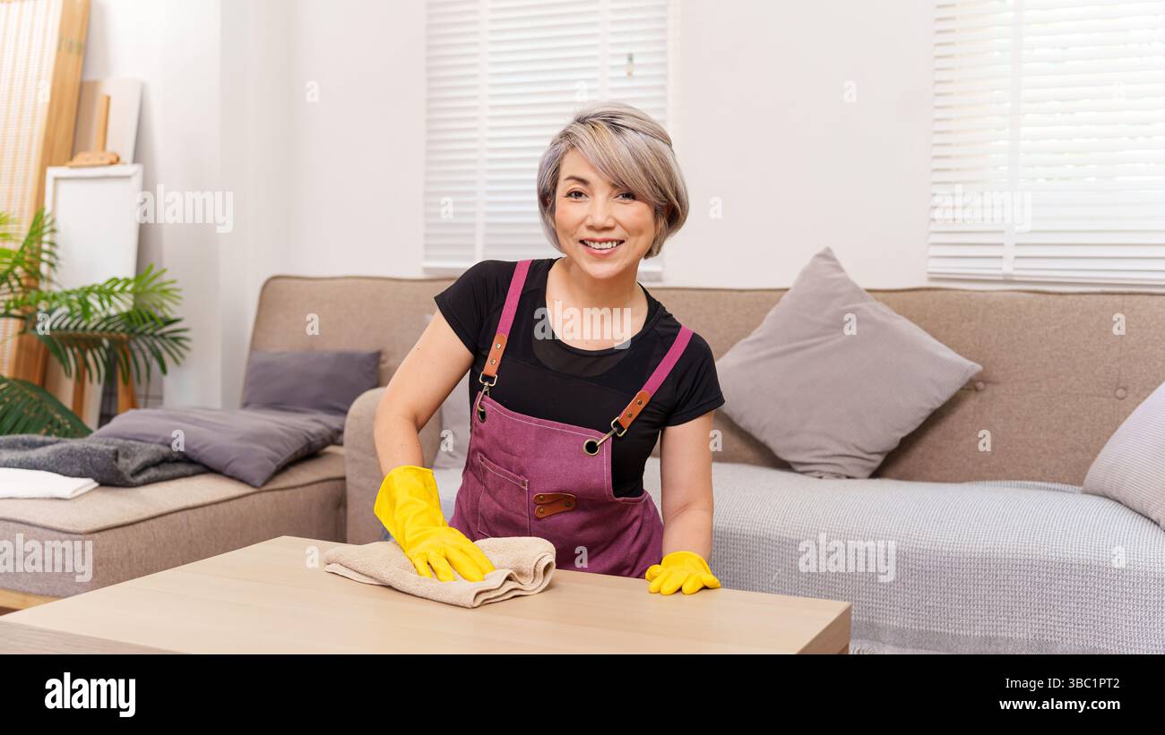 Image of an Asian adult woman cleaning a table in her living room. She ...