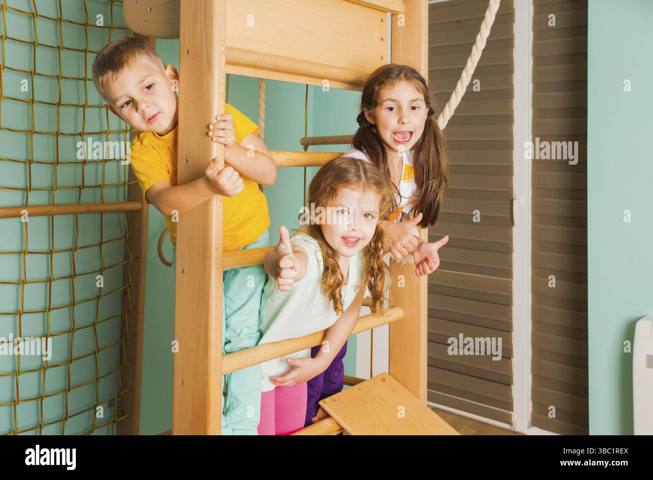 Portrait of cheerful smiling children on a wooden swedish wall, holding ...