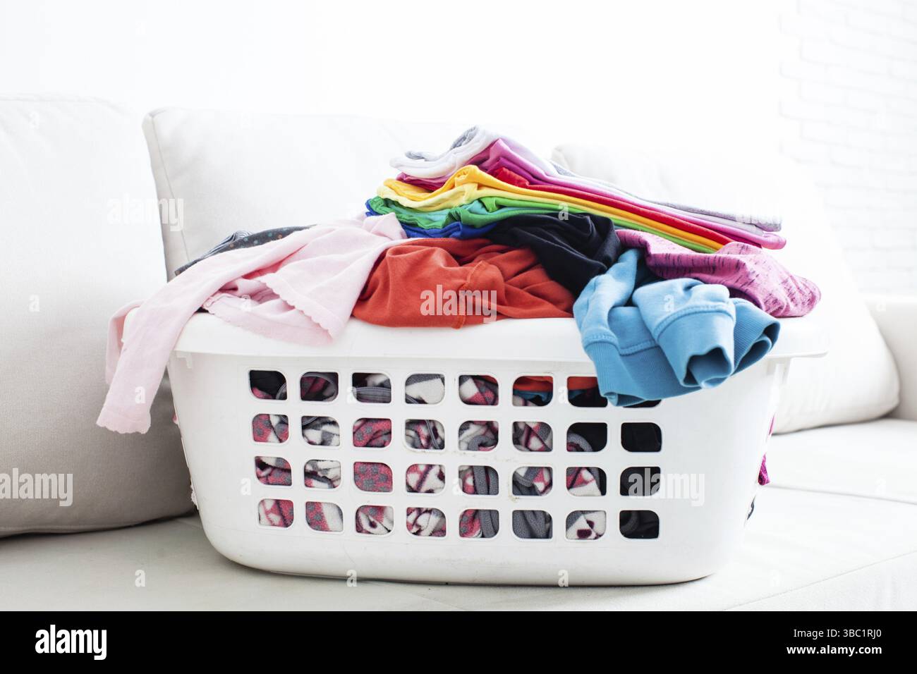 Washed clothes in a basket and stack of clean linen on the sofa Stock ...