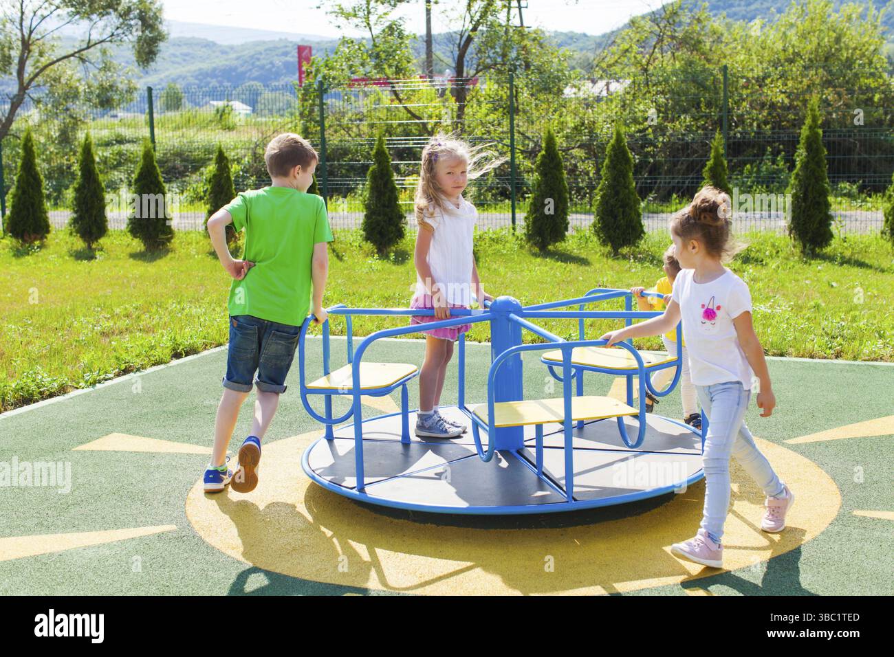 Little kids twist a carousel on a playground in the park Stock Photo ...