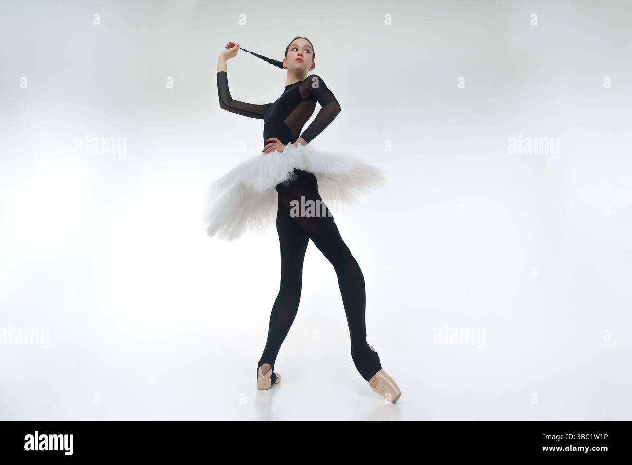 A young ballerina in a black leotard and tutu shows an eversion of her ...