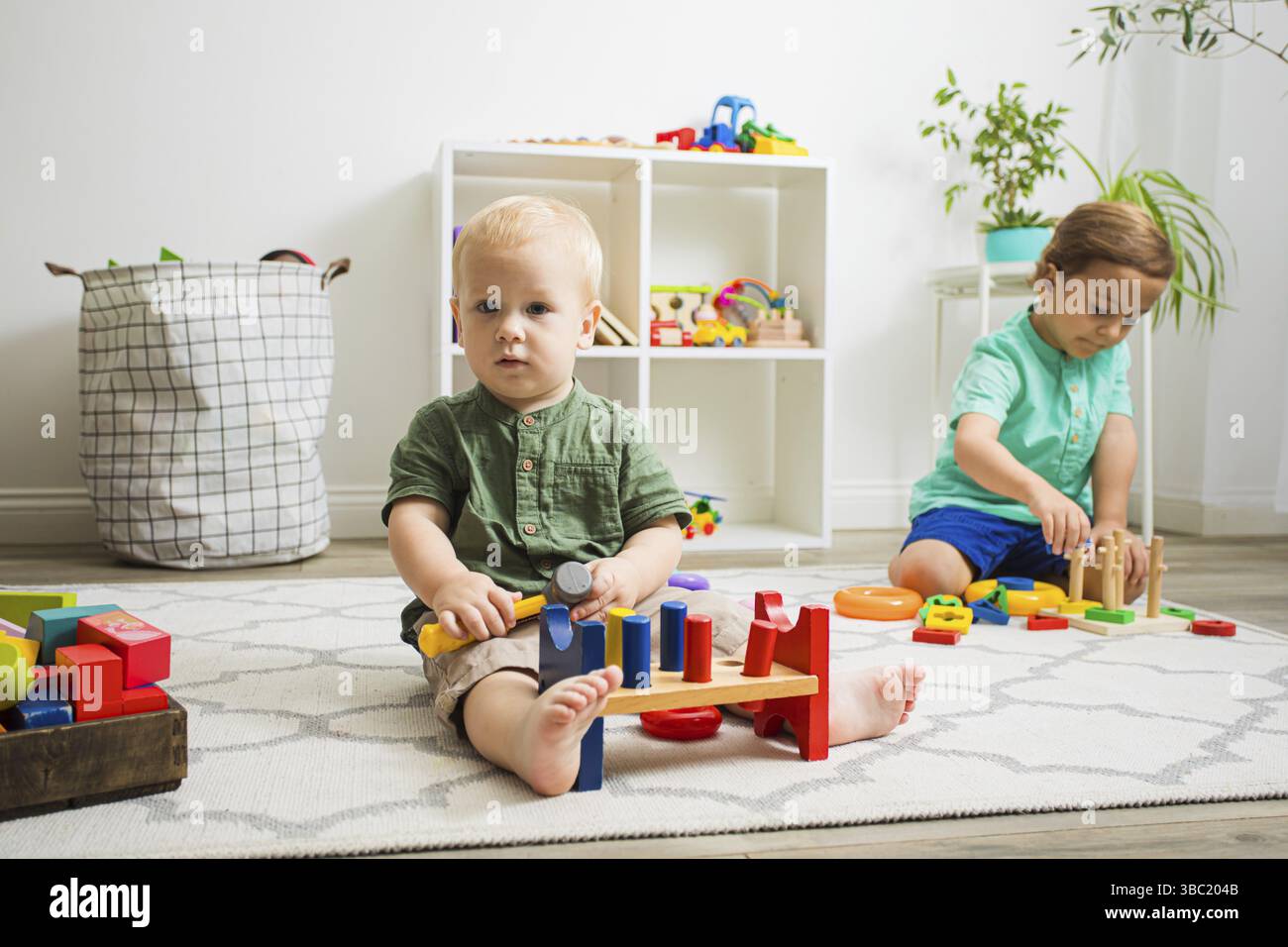 Cute toddler boy is playing with toy hammer, sitting on a floor in his ...