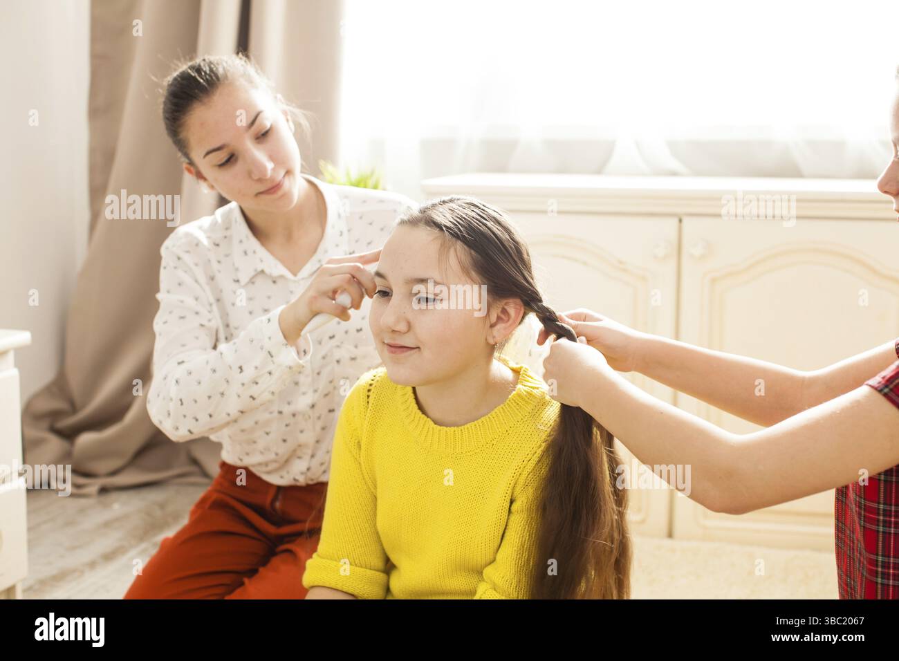 Three girls doing hair sitting on the floor in the room Stock Photo - Alamy