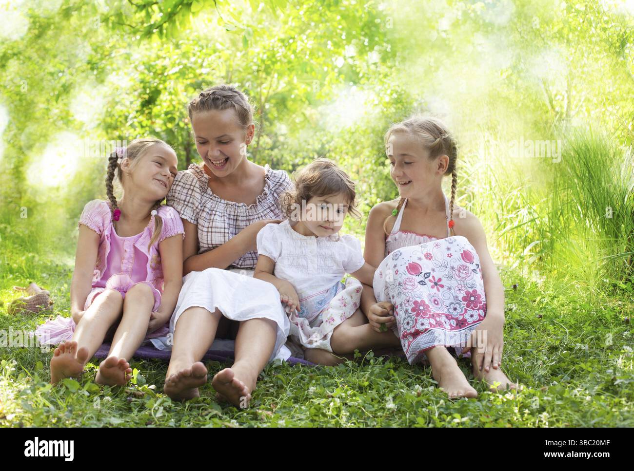 Four beautiful girls sitting on the grass in the garden and smiling ...