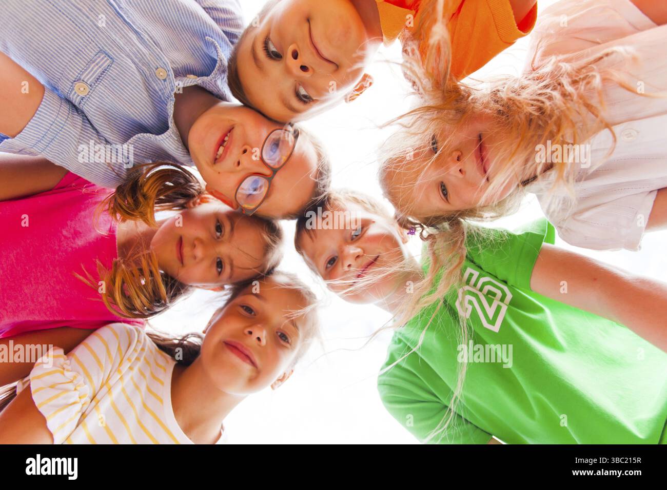 Cheerful kids of different age standing closely in a circle touching ...