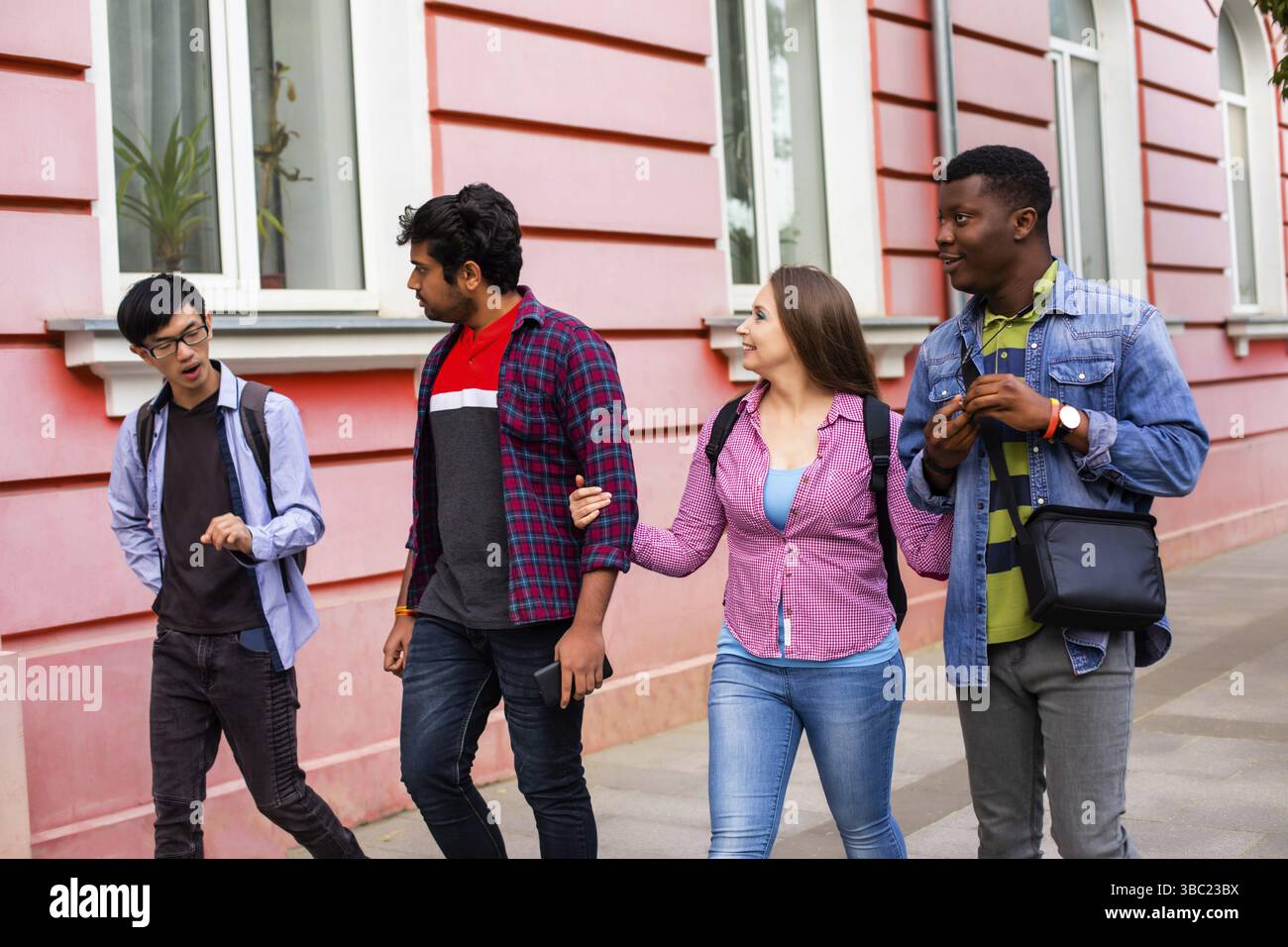 Four happy active young men and woman walking on street. Multiracial ...
