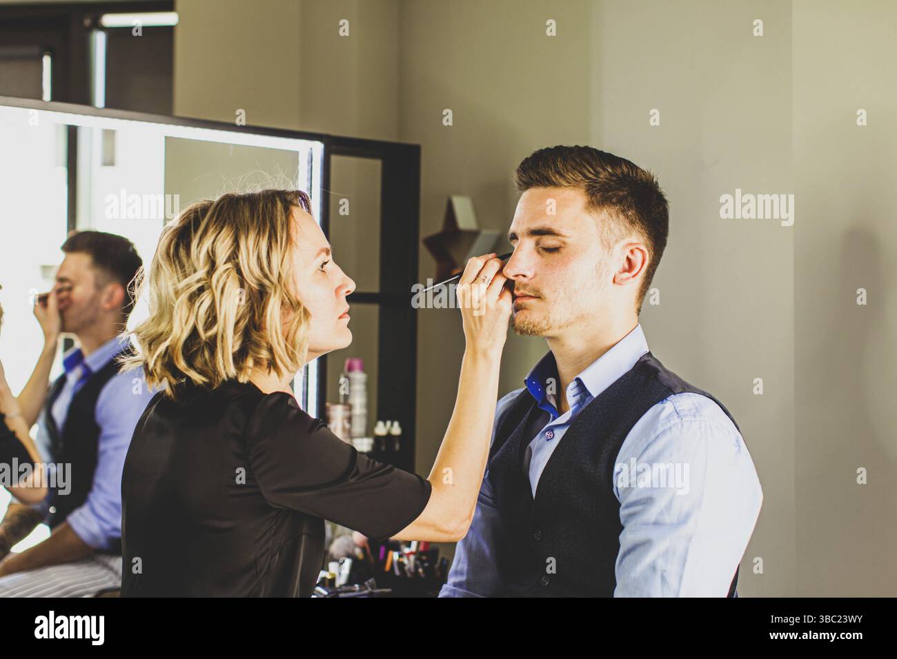 Makeup artist doing professional makeup for young man. Handsome model ...