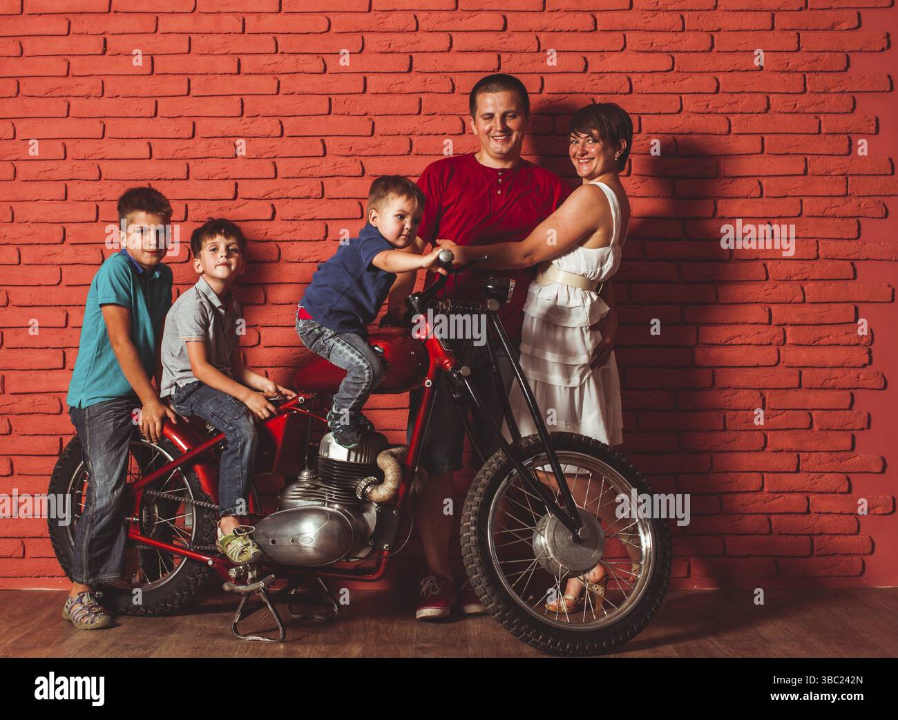Big and happy family on motorcycle at red background of brick wall ...