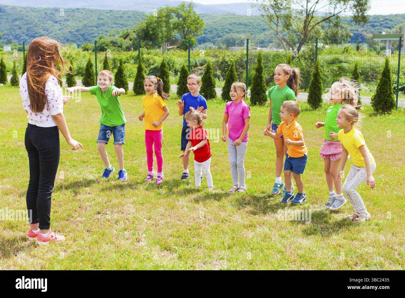 Children with teacher have fun outdoor on the green lawn in the summer ...