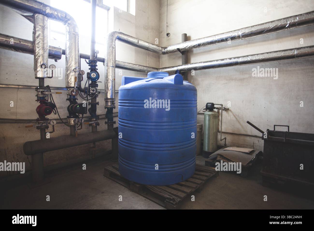 A large blue water barrel stands in the middle of the boiler room ...