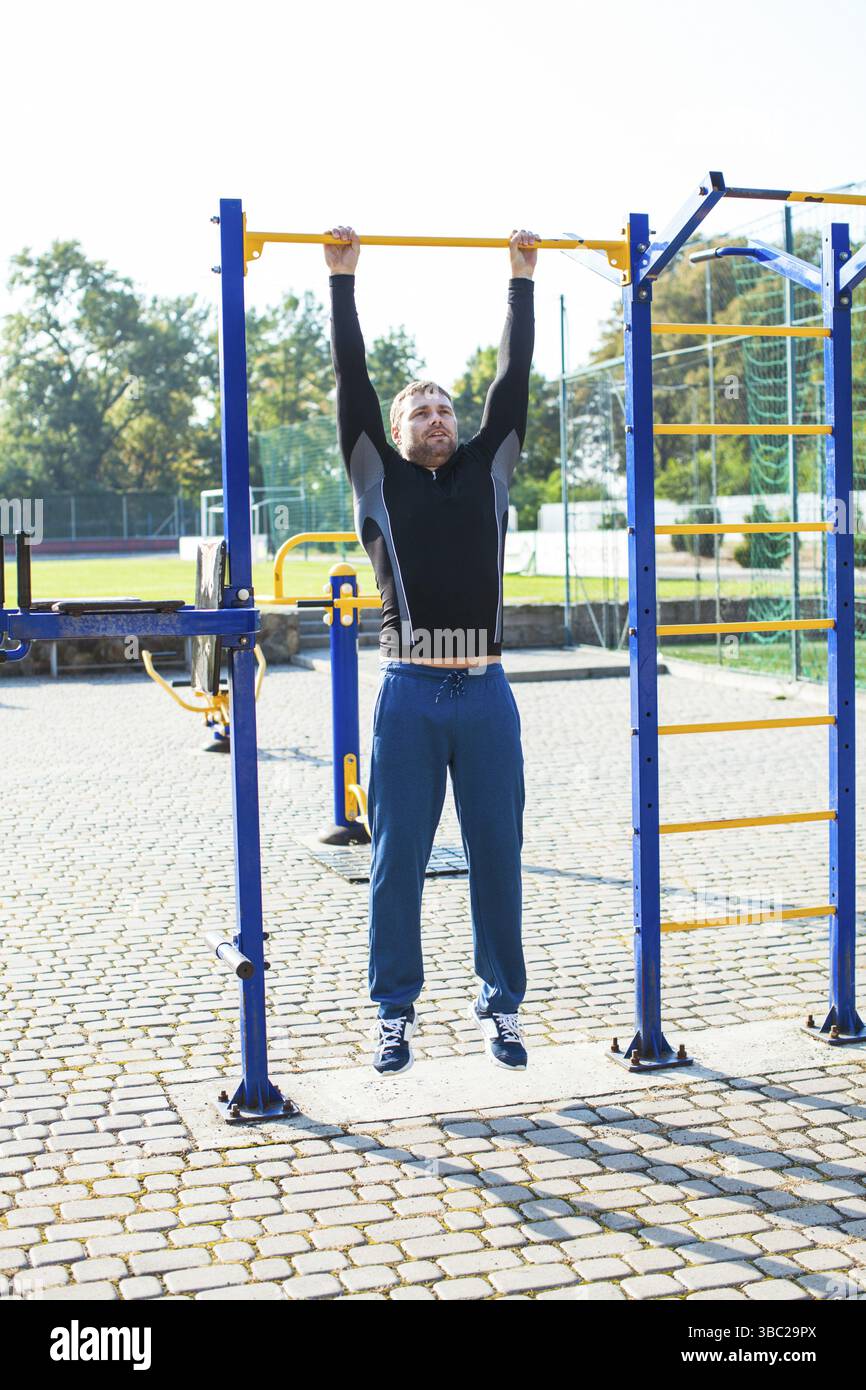 Man in sportswear performs pull-ups on the crossbar on a sports ground ...