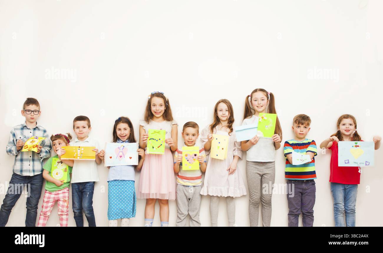 Happy kids showing their greeting card over white wall. Handmade paper ...