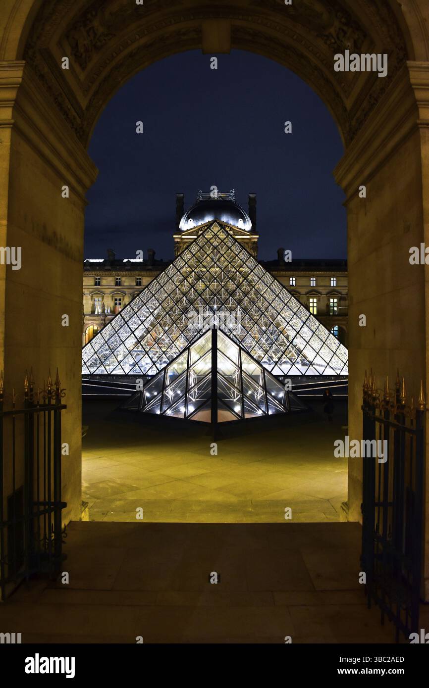 Louvre Pyramid illuminated at night seen through an archway in an ...