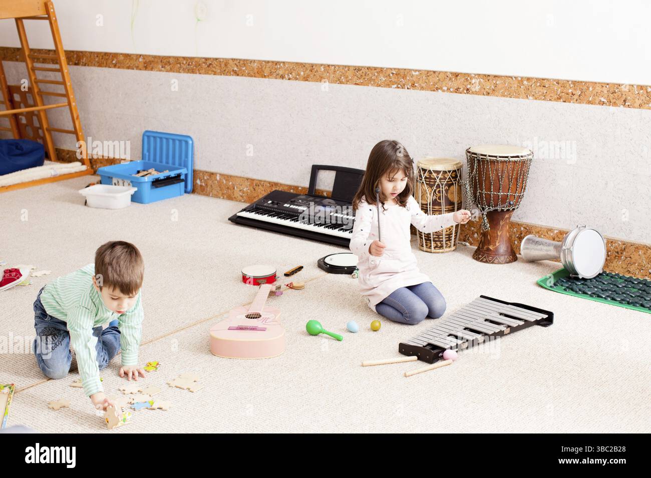 The cute little girl sits on the floor and playing on the xylophone at ...