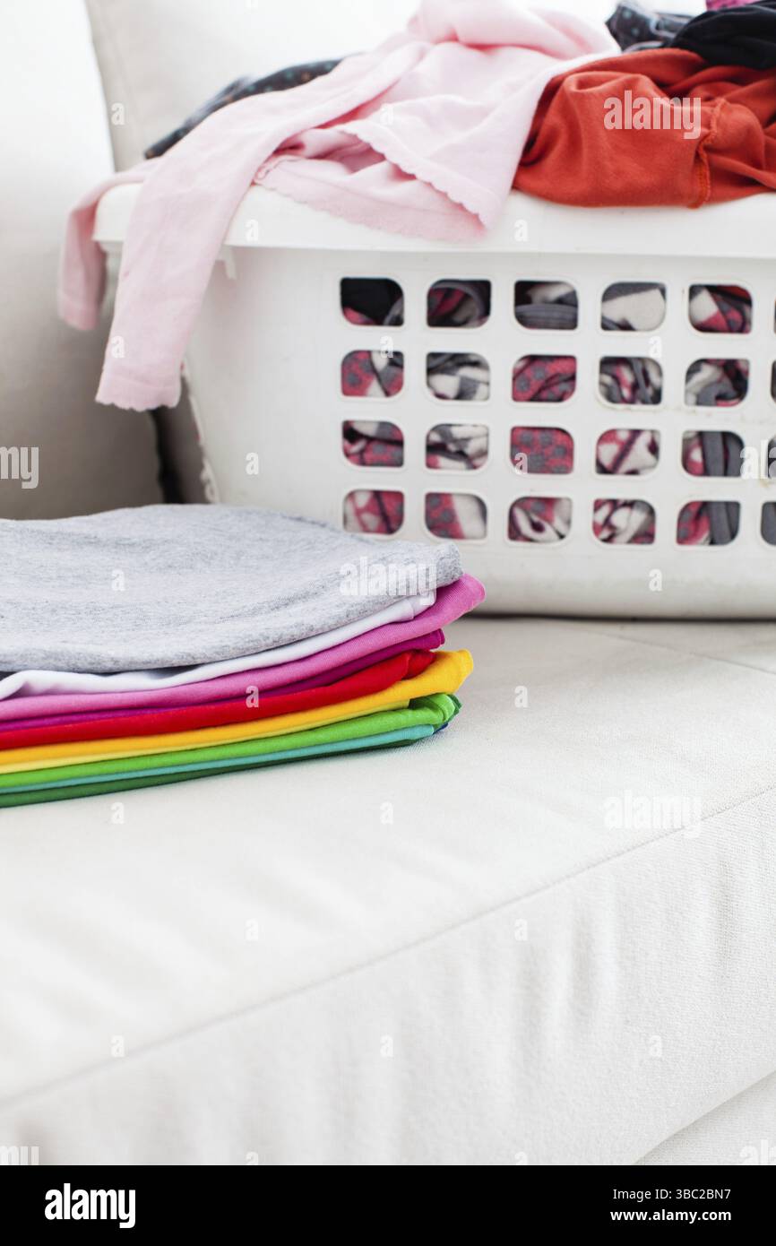 Washed clothes in a basket and stack of clean linen on the sofa Stock ...