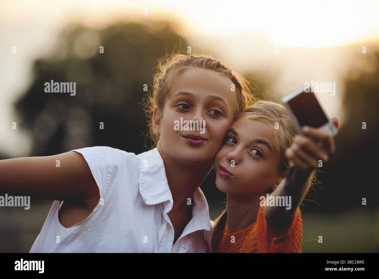 Friends taking a self portrait outdoor. Two girls makes selfie in the summer glow Stock Photo ...