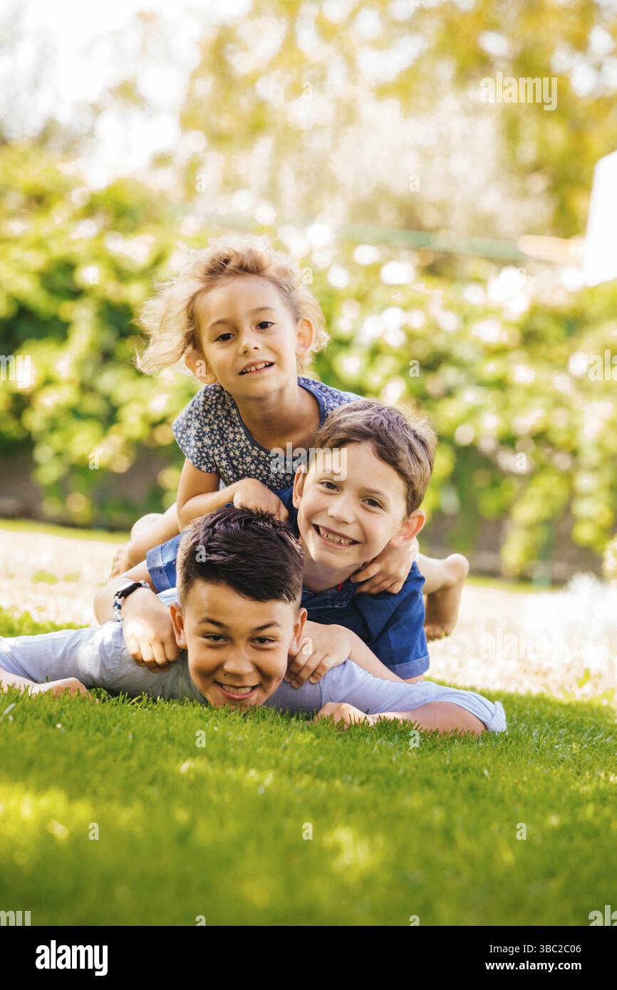 Portrait of three little children as a tower on a green grass. Playful ...