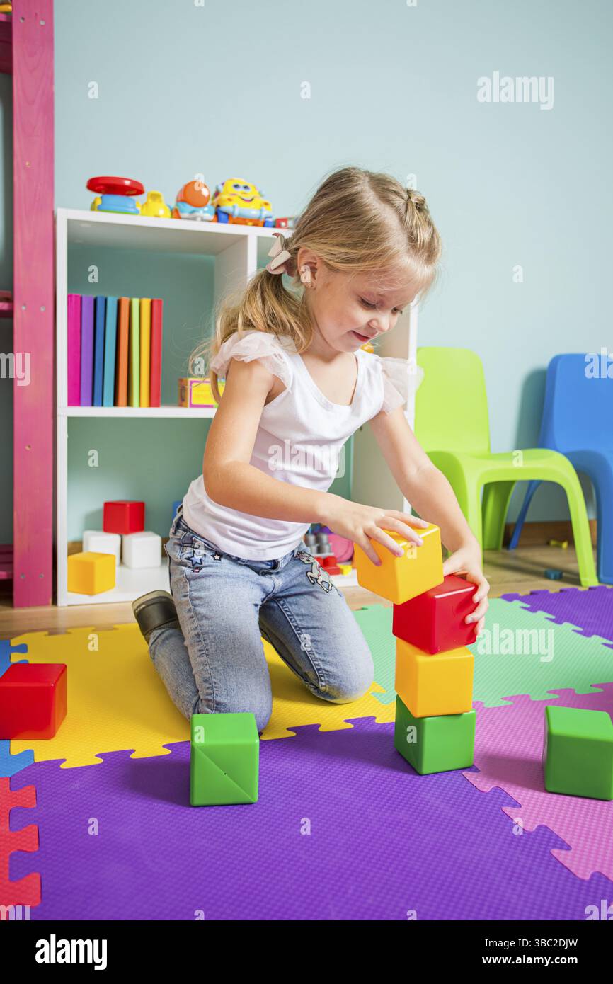 Beautiful preschool girl build tower from colorful bricks. Cheerful ...