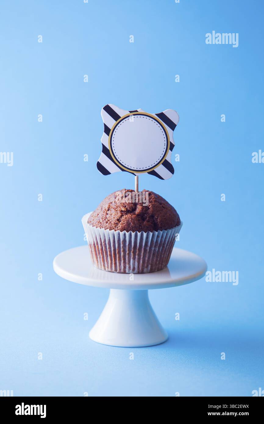 Tasty chocolate cupcake on white stand with round label cupcake topper ...