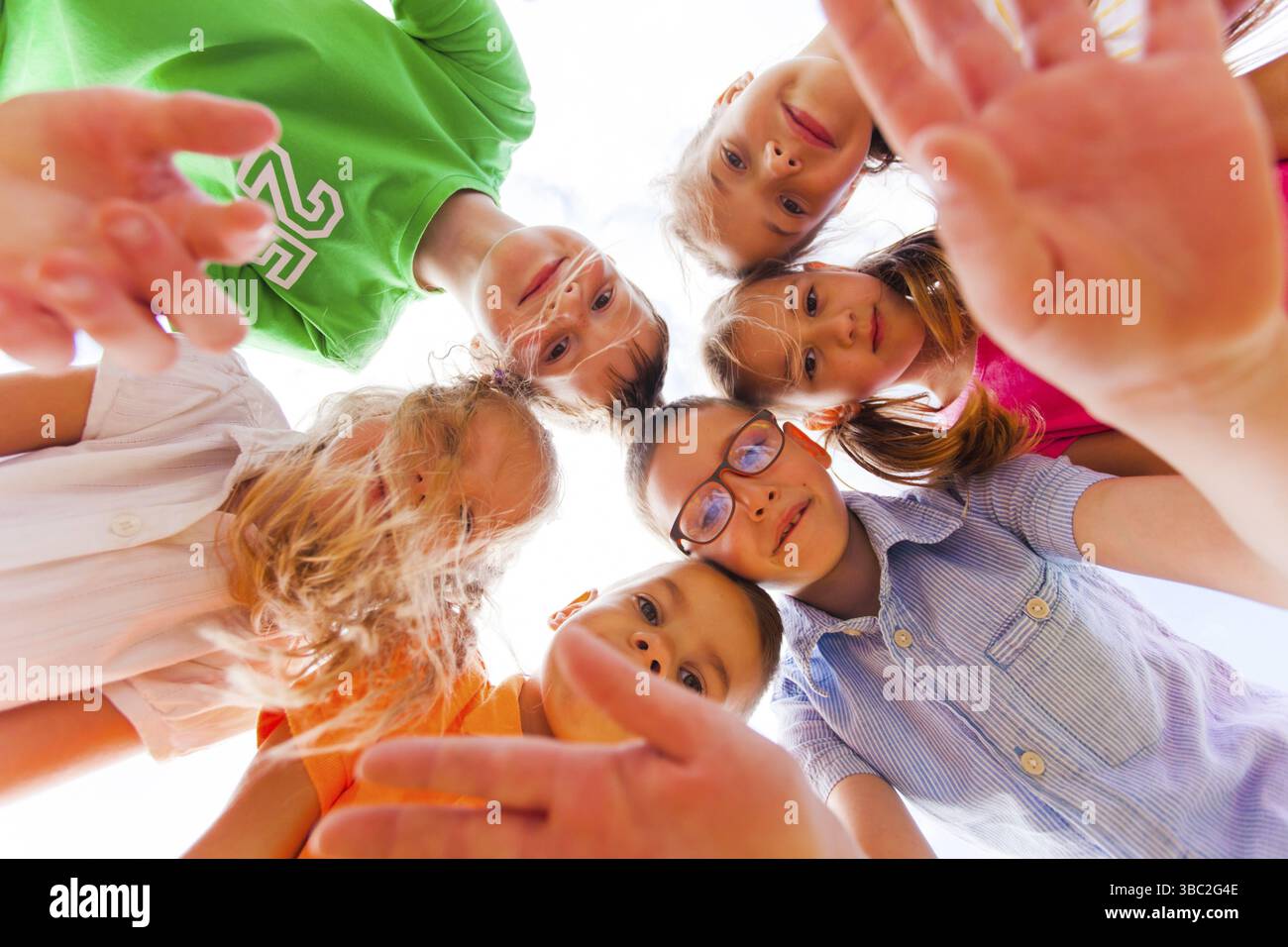 Cheerful kids of different age standing closely in a circle touching ...