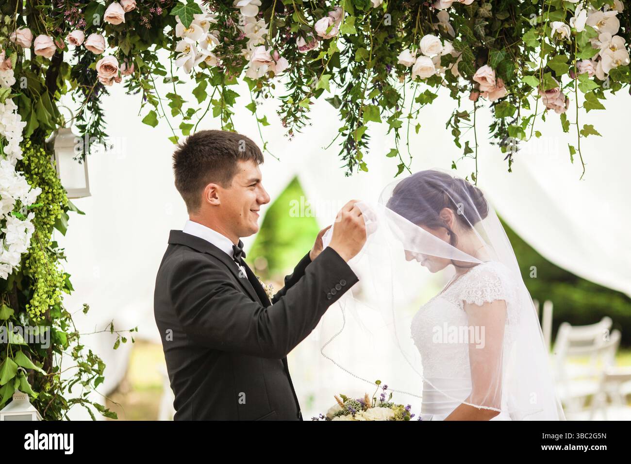 Wedding couple under the flower arch at the wedding ceremony outdoors ...