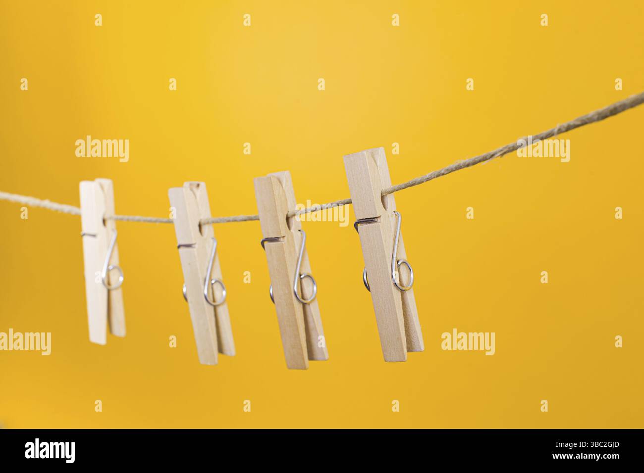 Wooden clothespins hanging on a rope over yellow background. Reusable ...