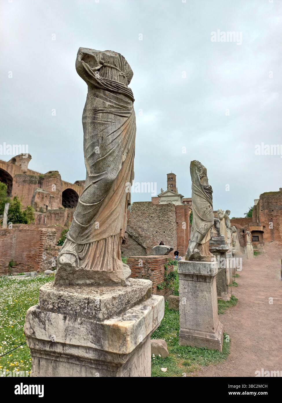 Rome, Lazio, Italy. April 15 2025. Ancient Roman statues without heads lined up in a grassy path ...