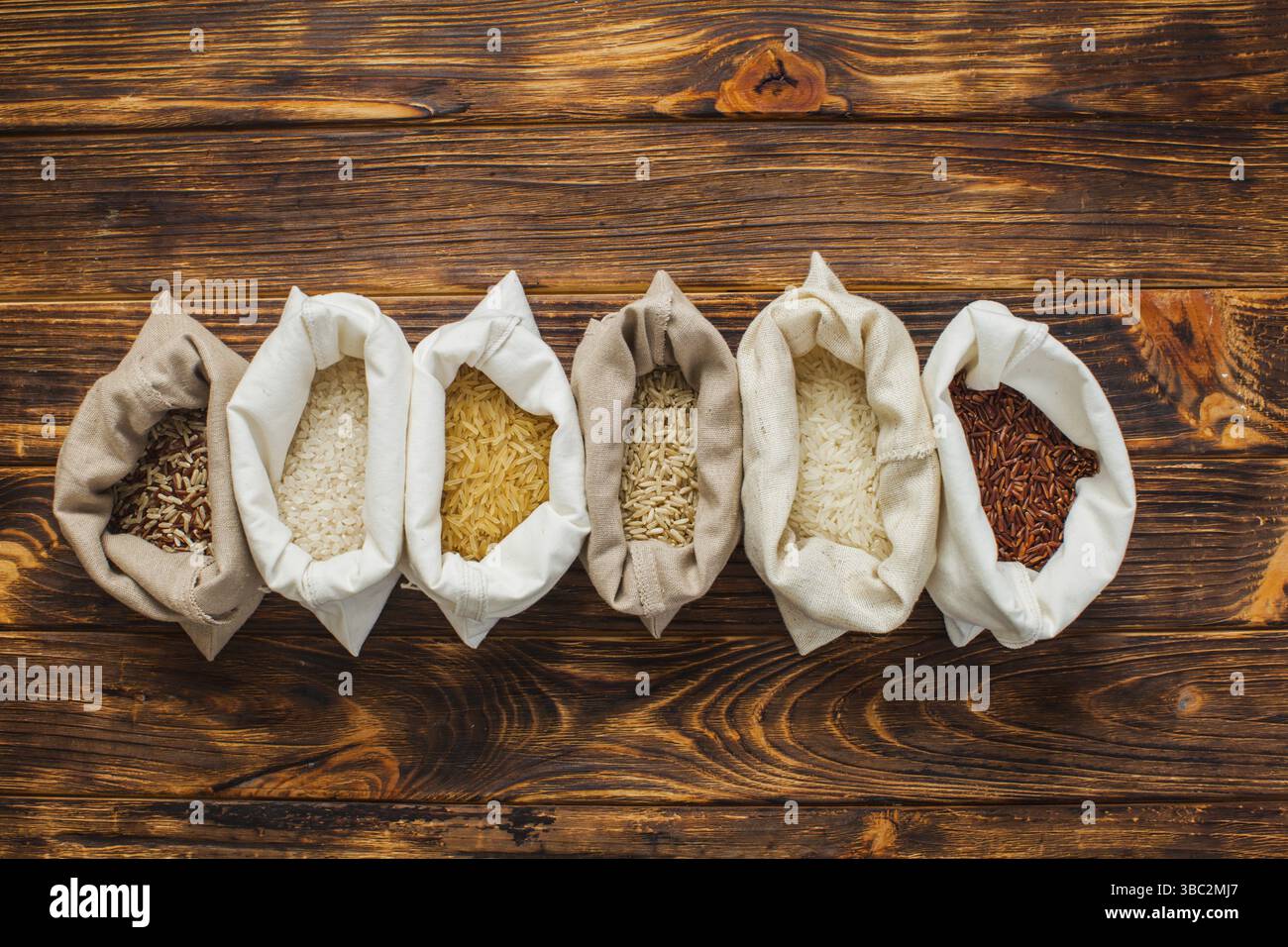 Different rice types in textile bags on wooden table. Top view, zero ...