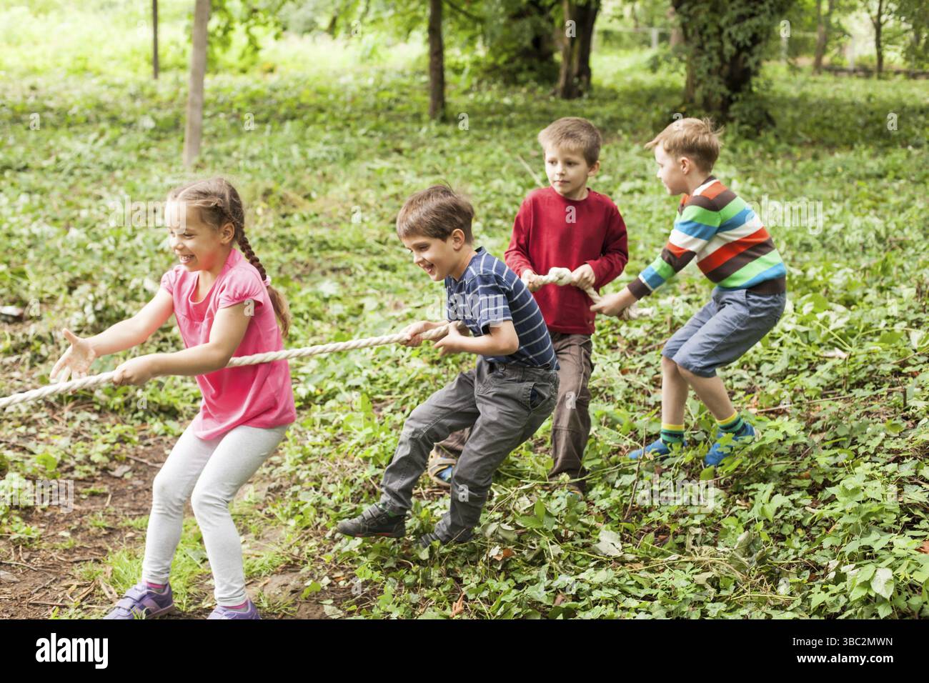 Group of happy smiling kids playing tug-of-war with rope in green park ...
