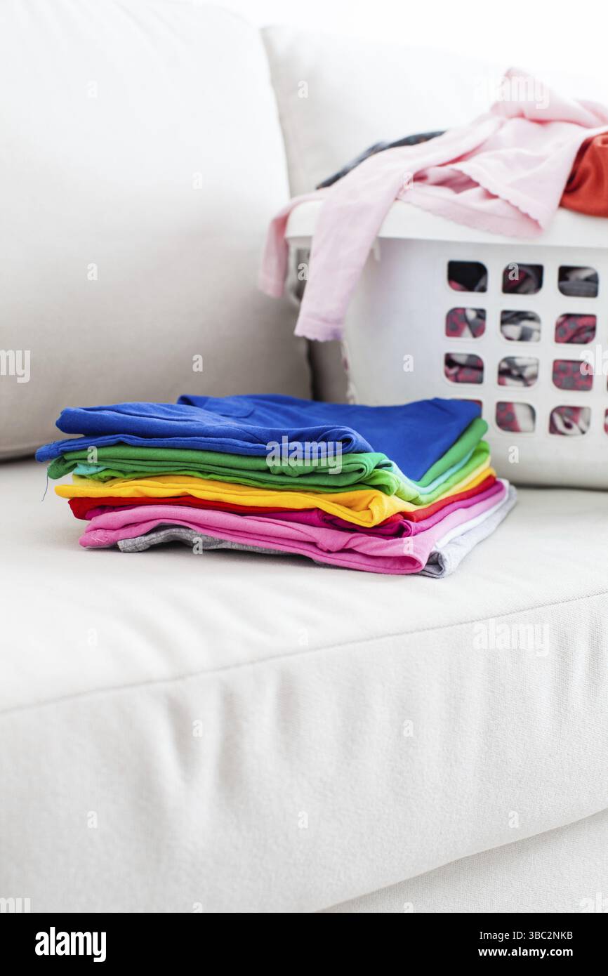 Washed clothes in a basket and stack of clean linen on the sofa Stock ...