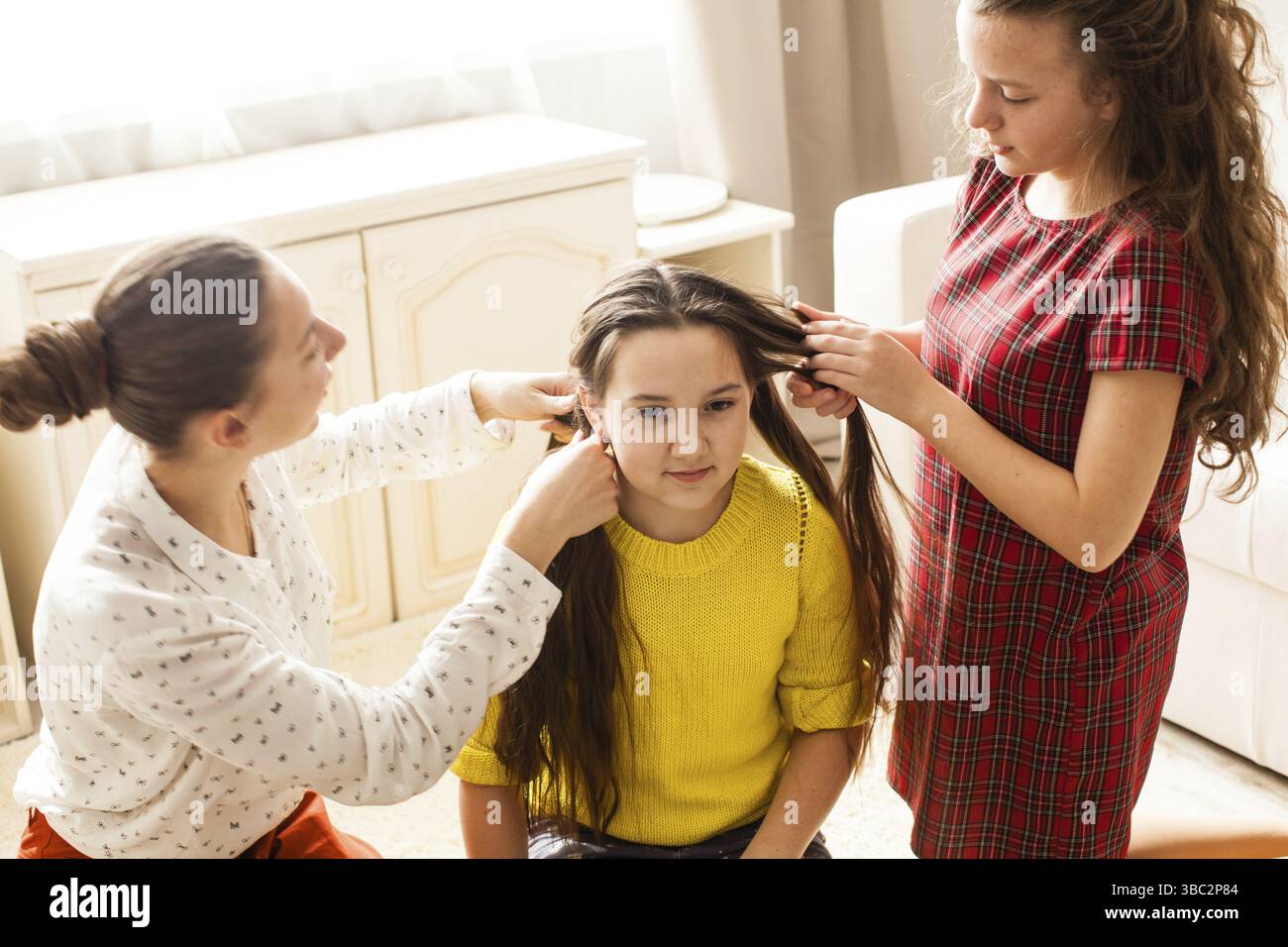 Three girls doing hair sitting on the floor in the room Stock Photo - Alamy
