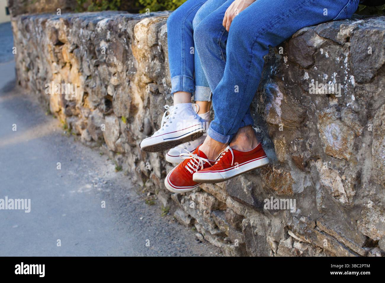 The legs of two people dressed in jeans and sneakers, hanging over a ...