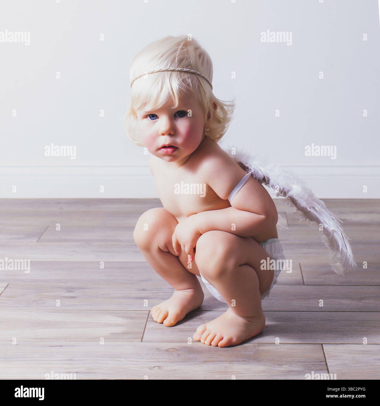 The baby blond boy with angel wings squatted in the room. The boy without clothes in a diaper is ...