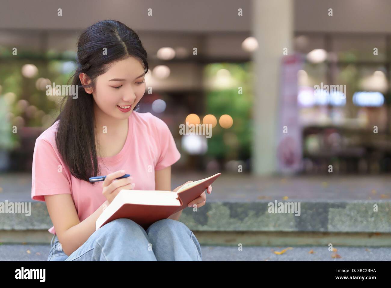 A young Asian woman is focused on learning and writing in her book ...