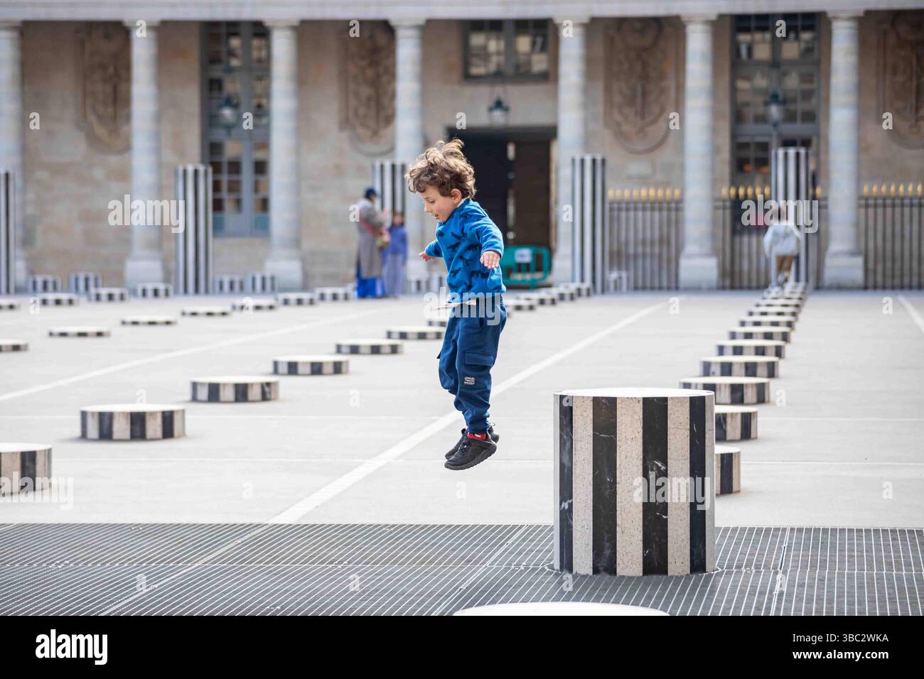 Boy jumping off black and white striped pillar of Les Deux Plateaux or ...