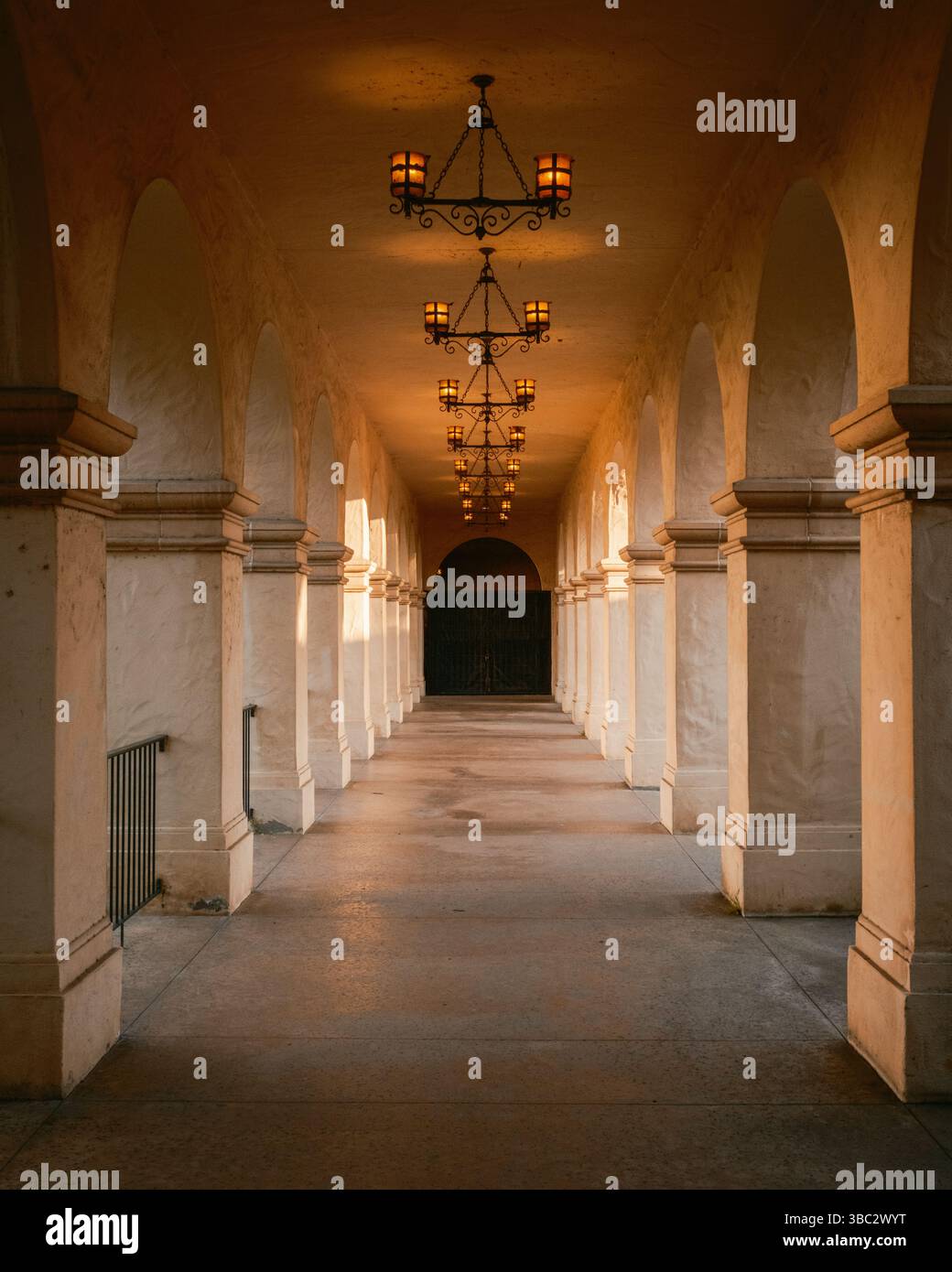 Hallway with a series of arches and hanging lights leads to a gated ...