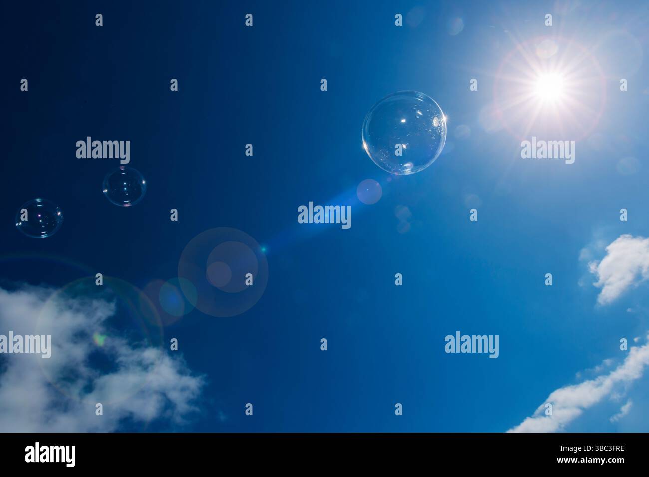 Soap bubbles in the blue sky with isolated clouds backlit by the sun ...